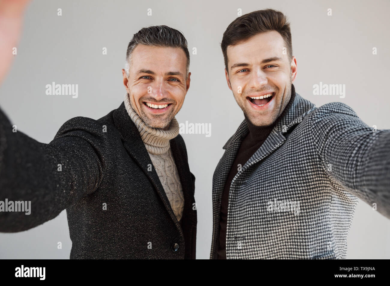 Two handsome men wearing coats over gray background, taking a selfie ...