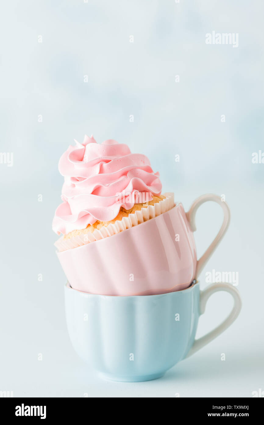Cupcake with gentle pink cream decoration in two cups on blue pastel ...