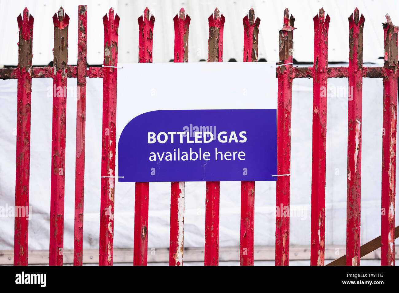 Bottled gas available here sign on red railing fence Stock Photo - Alamy