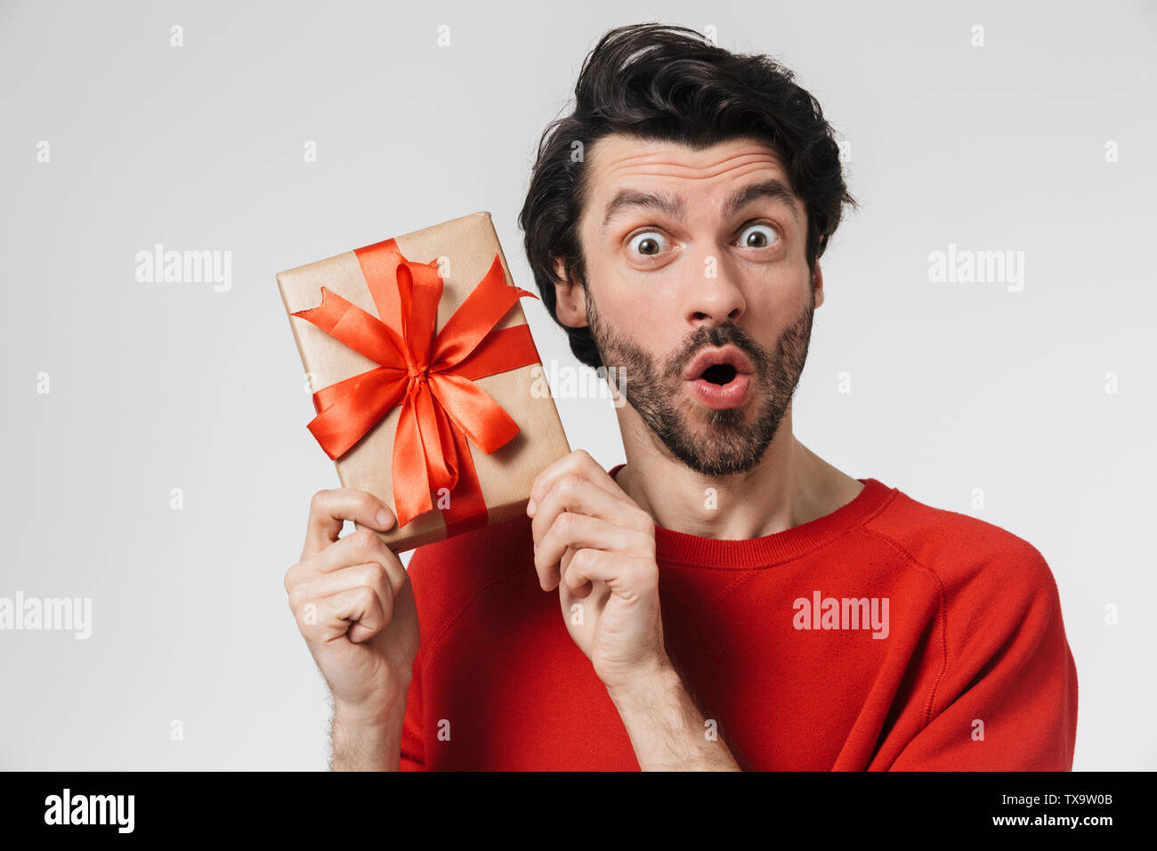 Handsome excited young bearded brunette man wearing sweater standing isolated over white ...