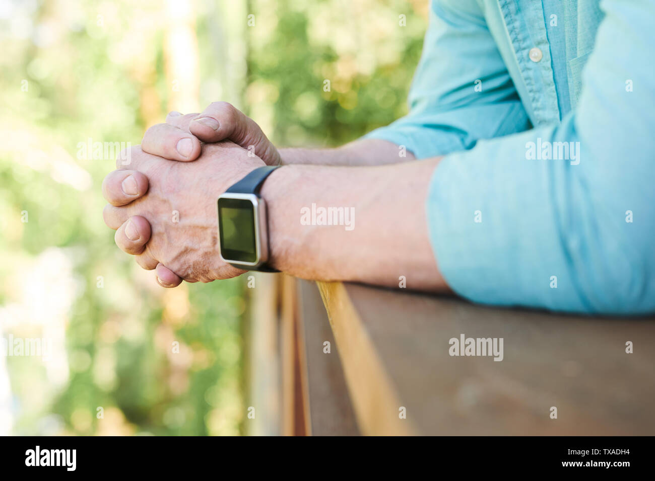 Hands of restful man with wristwatch leaning against wooden banisters ...