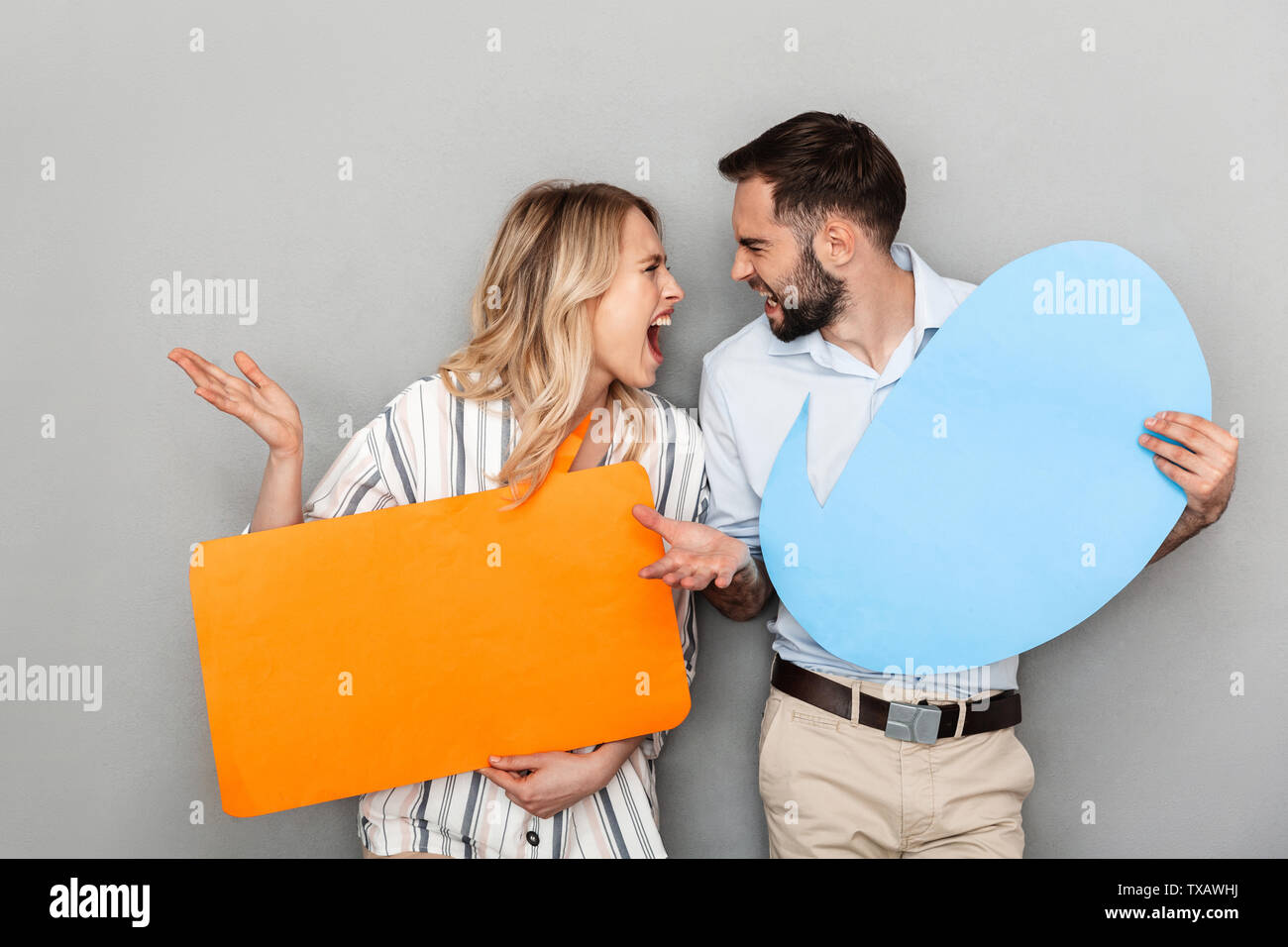 Attractive angry young couple standing isolated over gray background ...
