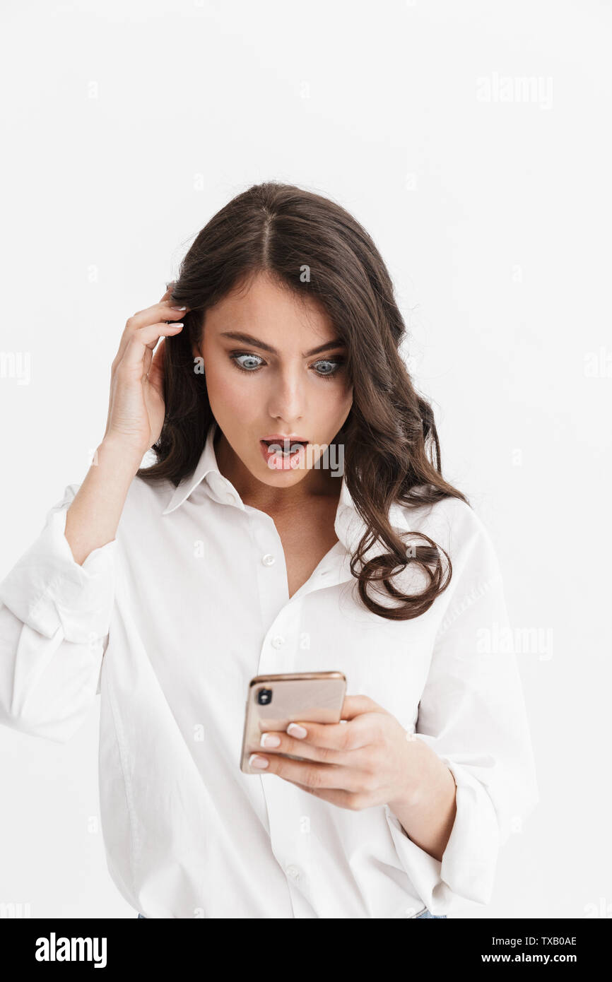 Beautiful young woman with long curly brunette hair wearing white shirt standing isolated over ...