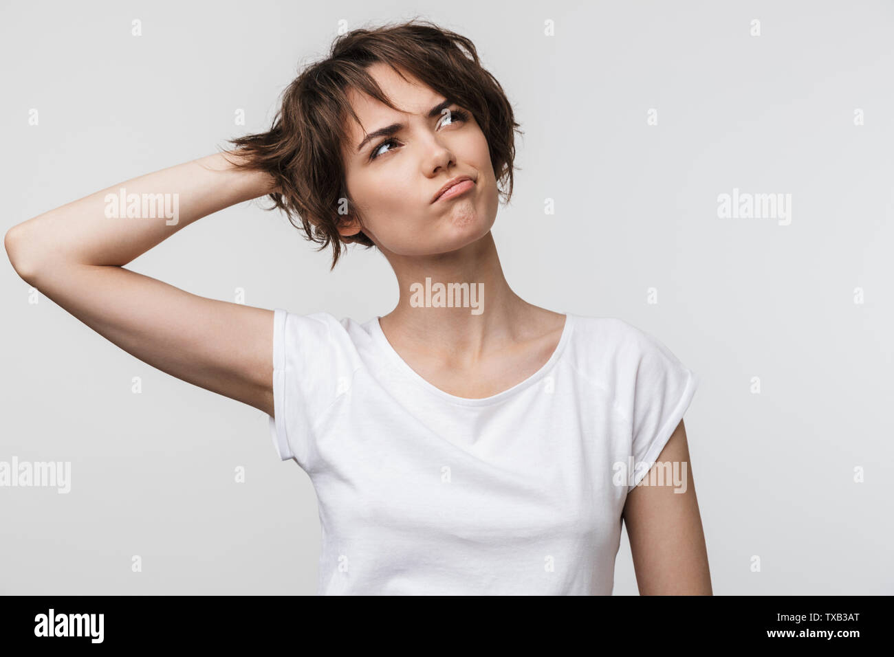 Portrait of young woman with short brown hair in basic t-shirt frowning ...