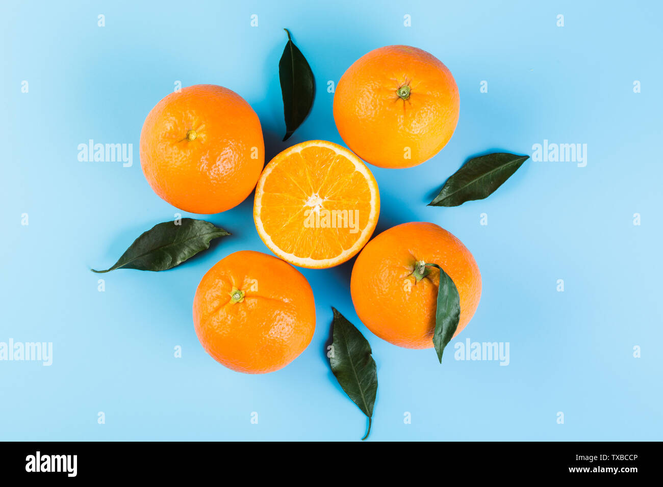 Fresh cut oranges and green leaves on blue background, overhead shot ...