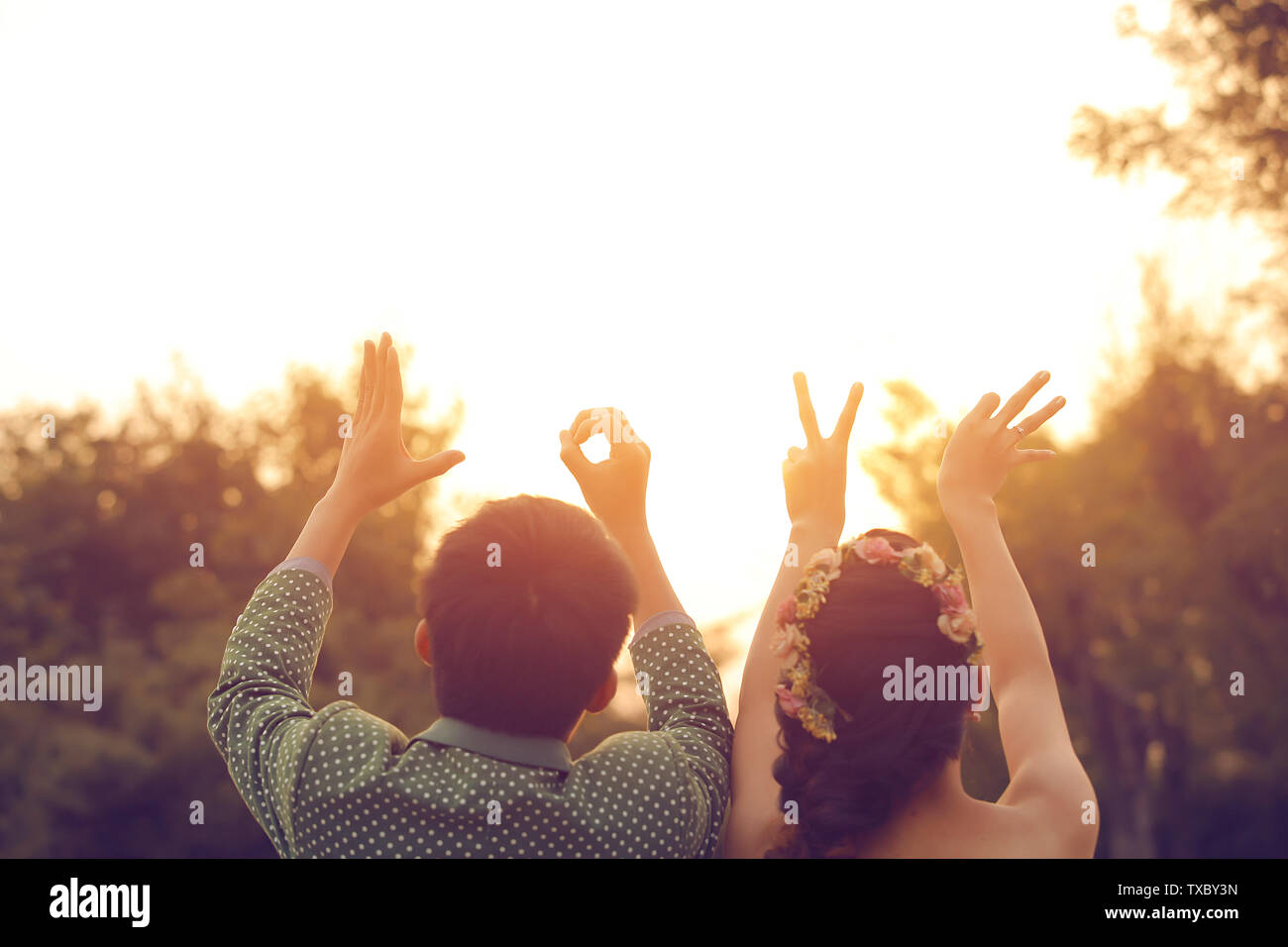 In the setting sun, a couple poses a love shape with their hands and a ...