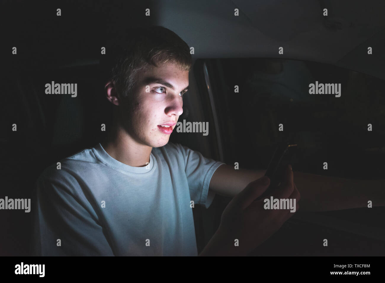 Distracted teenager driving a car with his cell phone in his hand. The ...