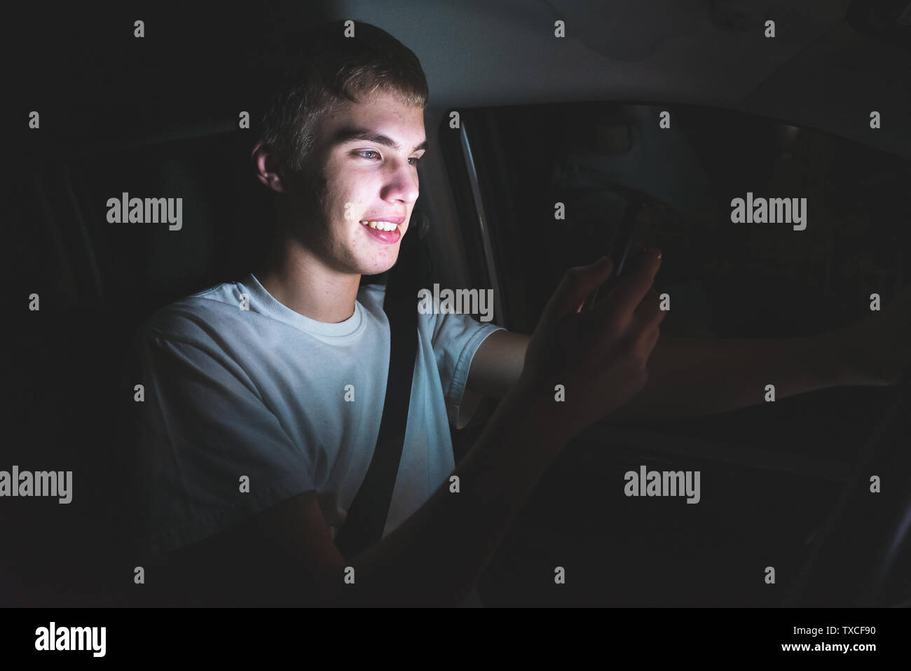 Distracted teenager driving a car with his cell phone in his hand. The ...