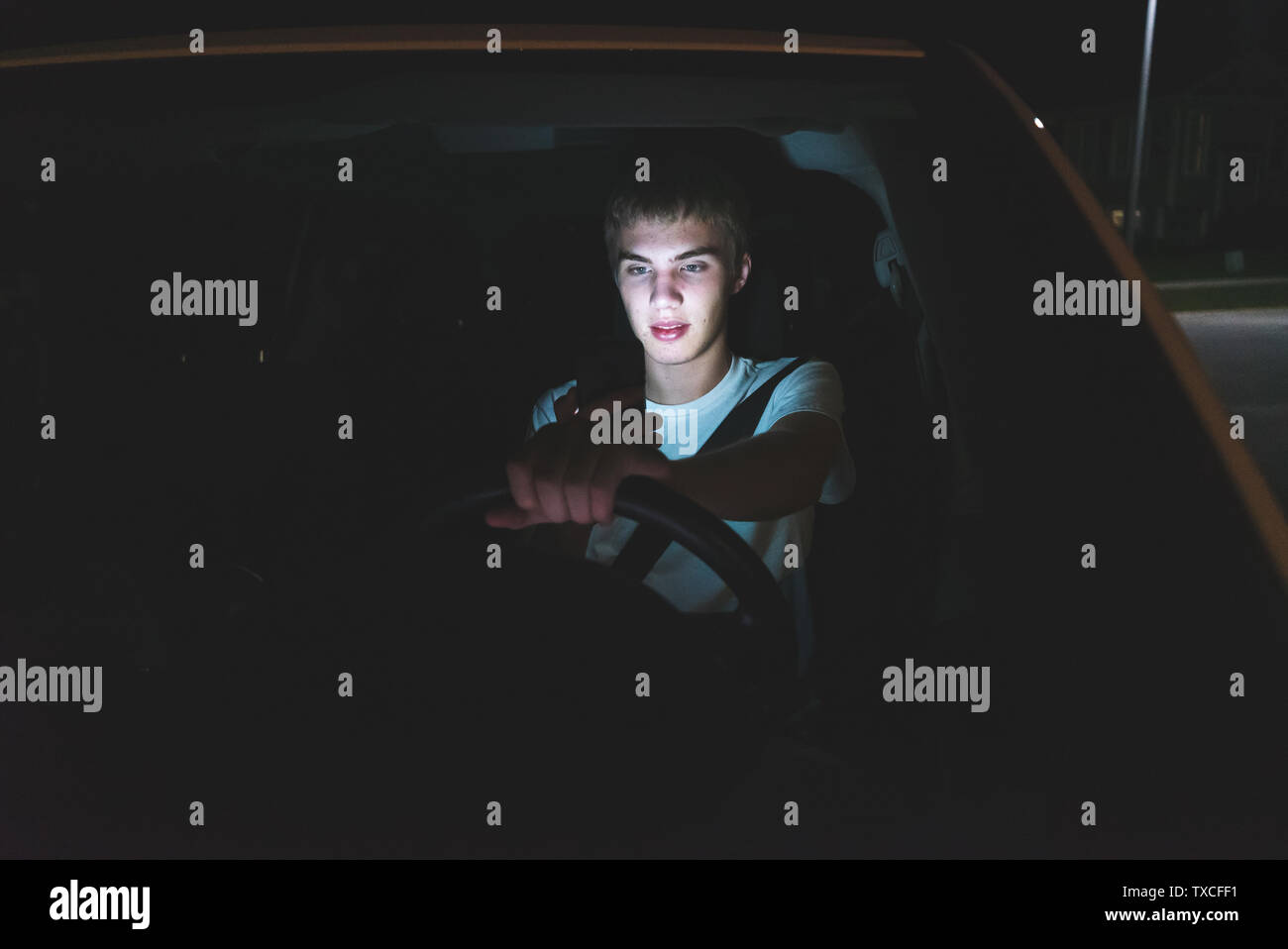 Distracted teenager driving a car with his cell phone in his hand. The ...