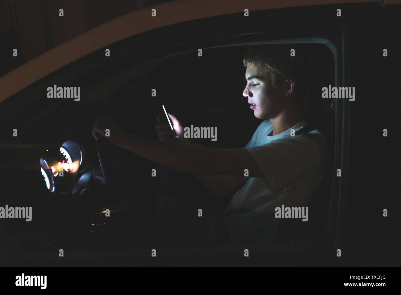 Distracted teenager driving a car with his cell phone in his hand. The ...