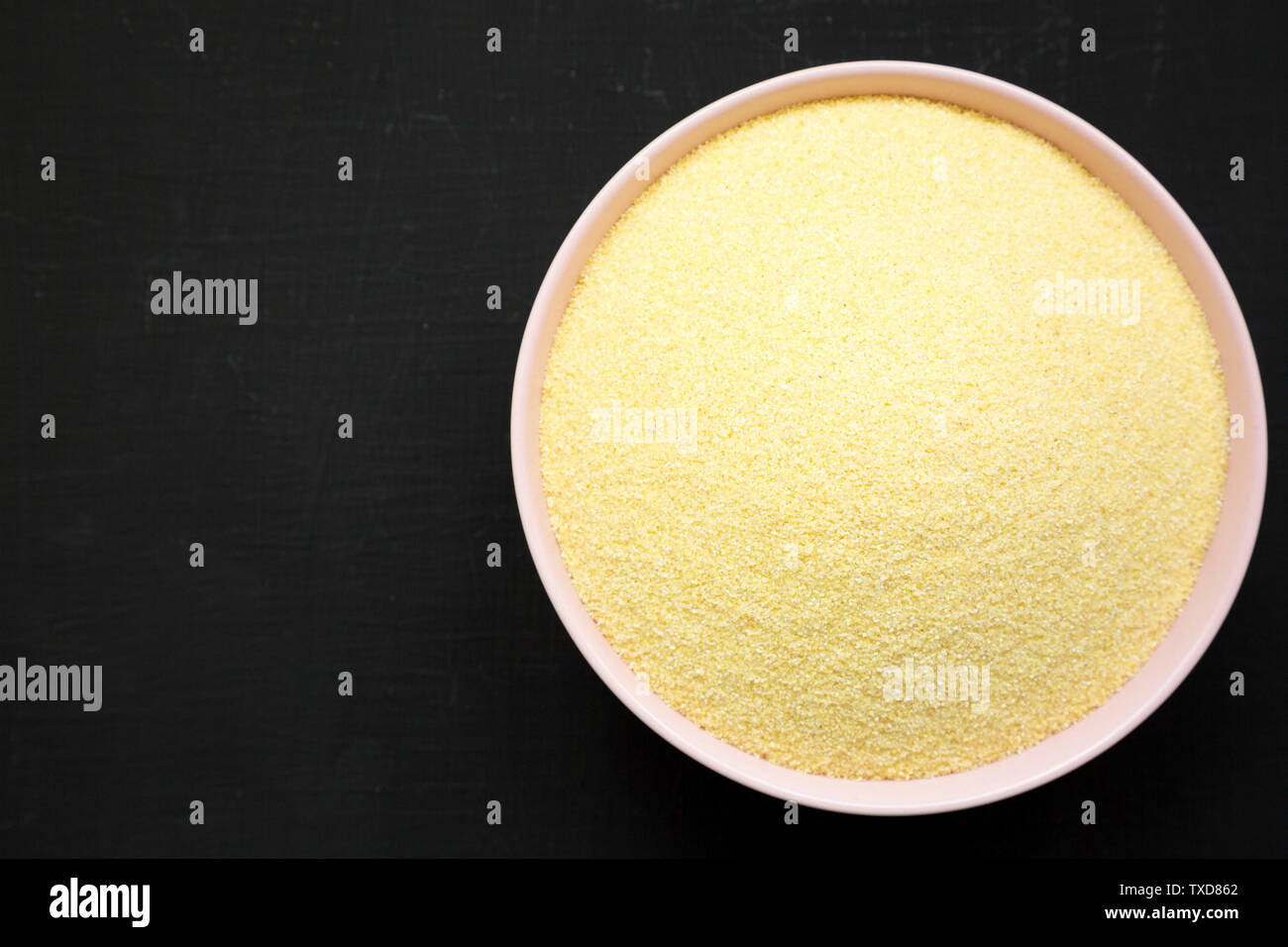 Dry semolina durum flour in a pink bowl over black background, top view ...