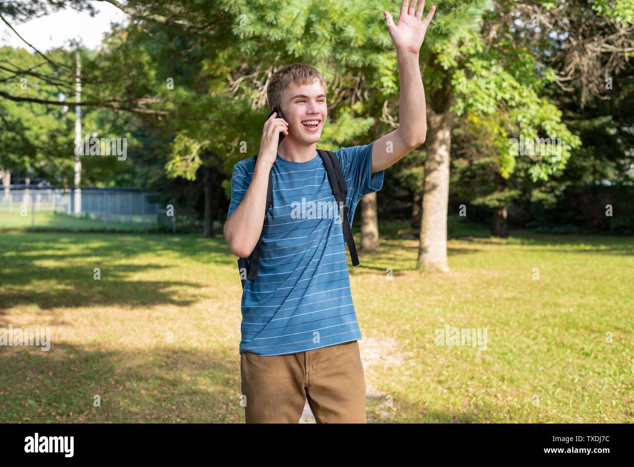 Happy teenager waving to his friends as he is talking on his cellphone ...