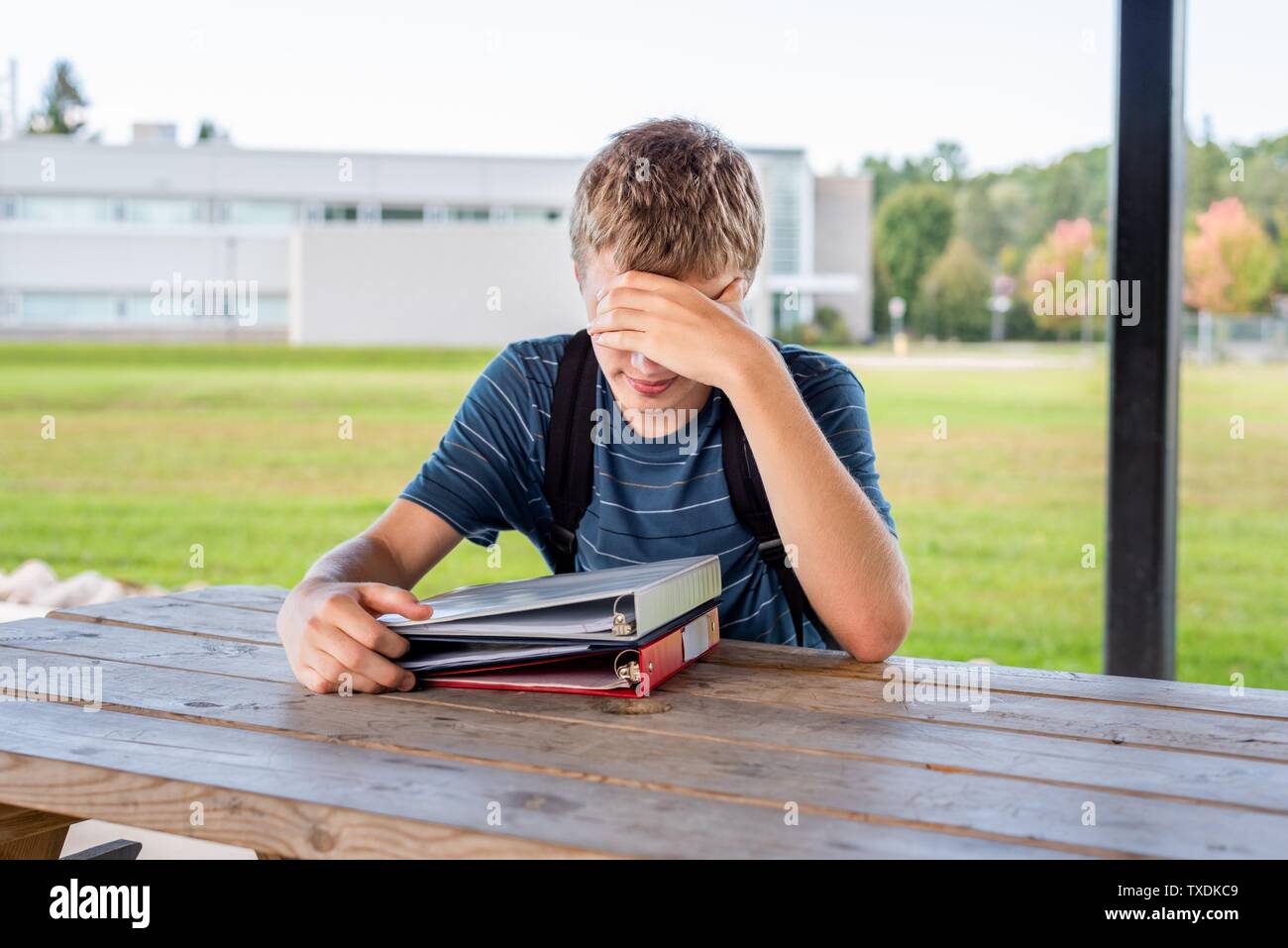 Bored teenager reluctant to do his homework while sitting at an outdoor table Stock Photo - Alamy