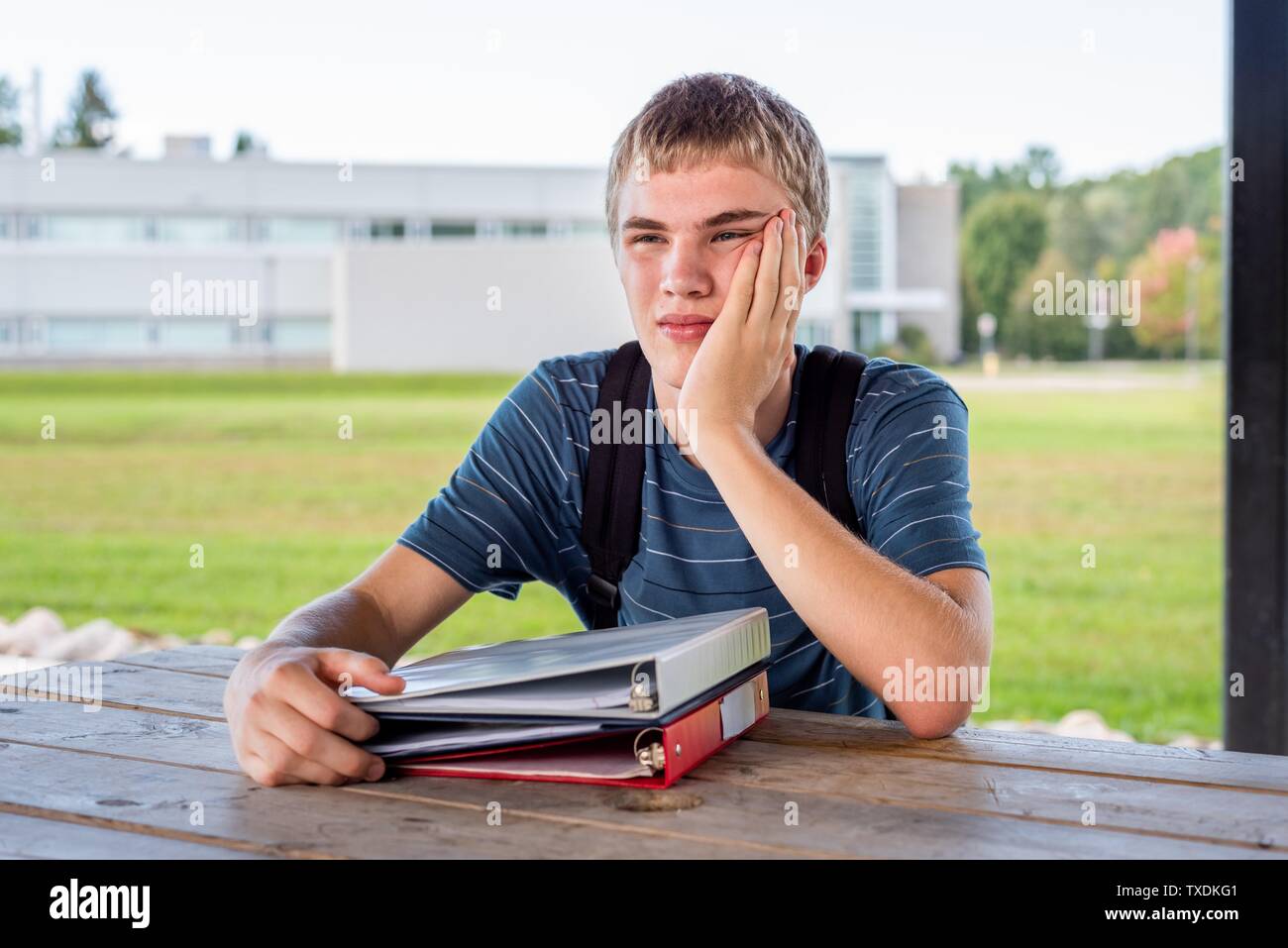 Bored teenager reluctant to do his homework while sitting at an outdoor table Stock Photo - Alamy
