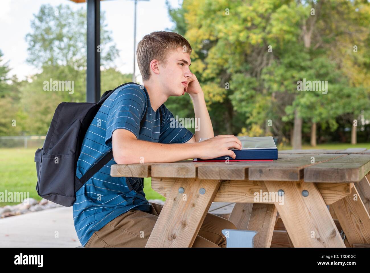 Bored teenager reluctant to do his homework while sitting at an outdoor ...