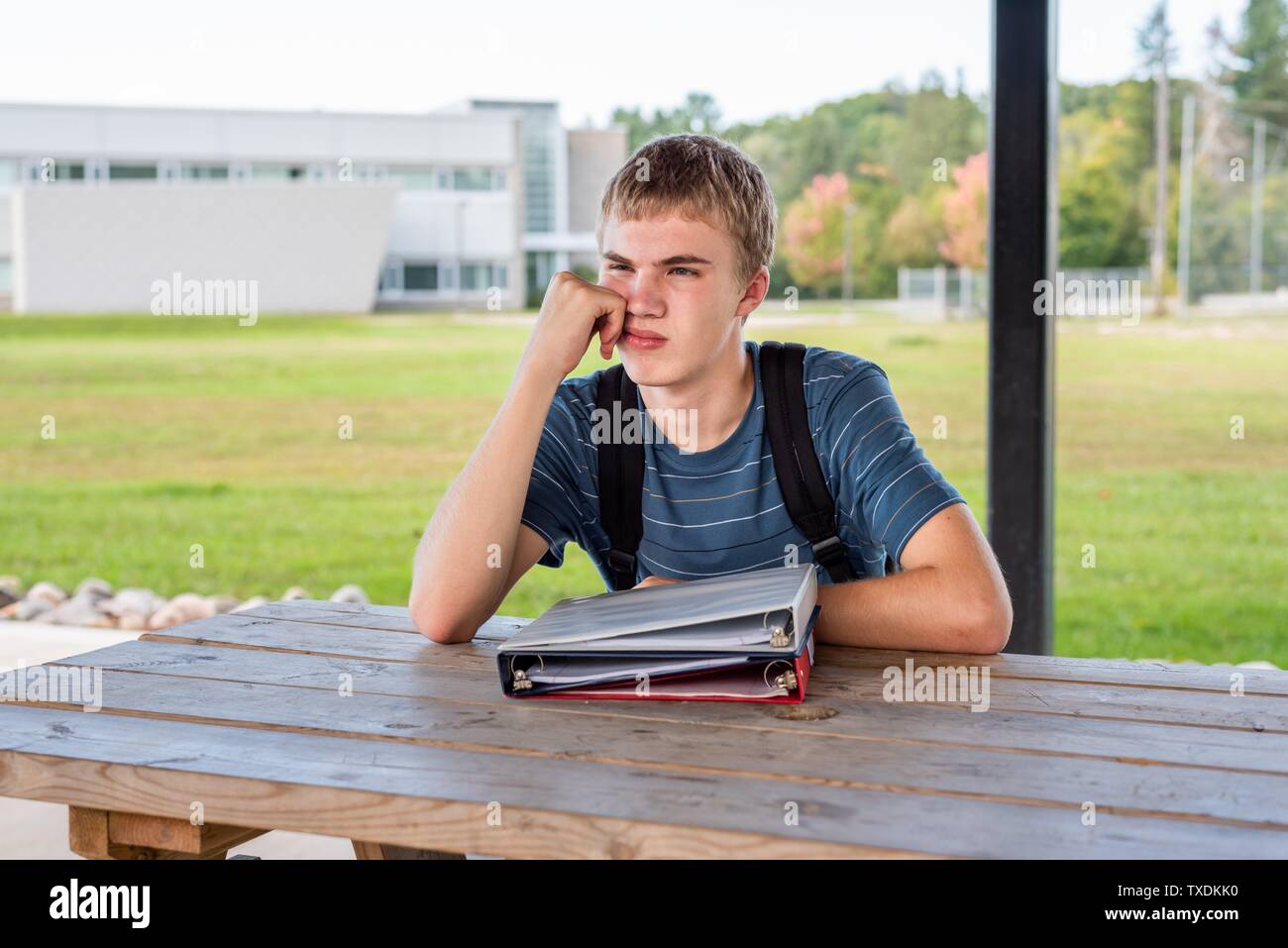 Bored teenager reluctant to do his homework while sitting at an outdoor table Stock Photo - Alamy