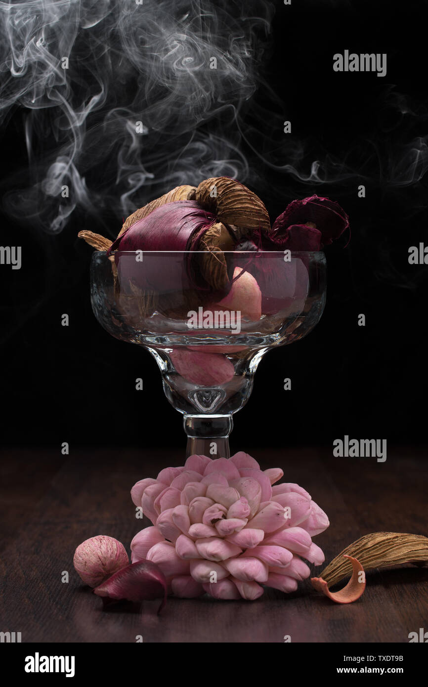 Glass filled with brown, pink and red potpourri and pink flower with ...