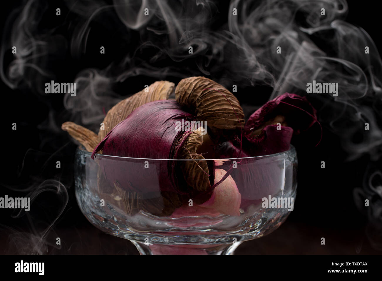 Glass filled with brown, pink and red potpourri with smoke with black ...