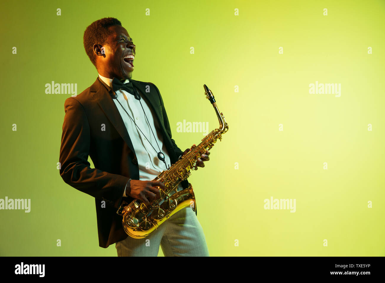Young african-american jazz musician playing the saxophone on gradient ...