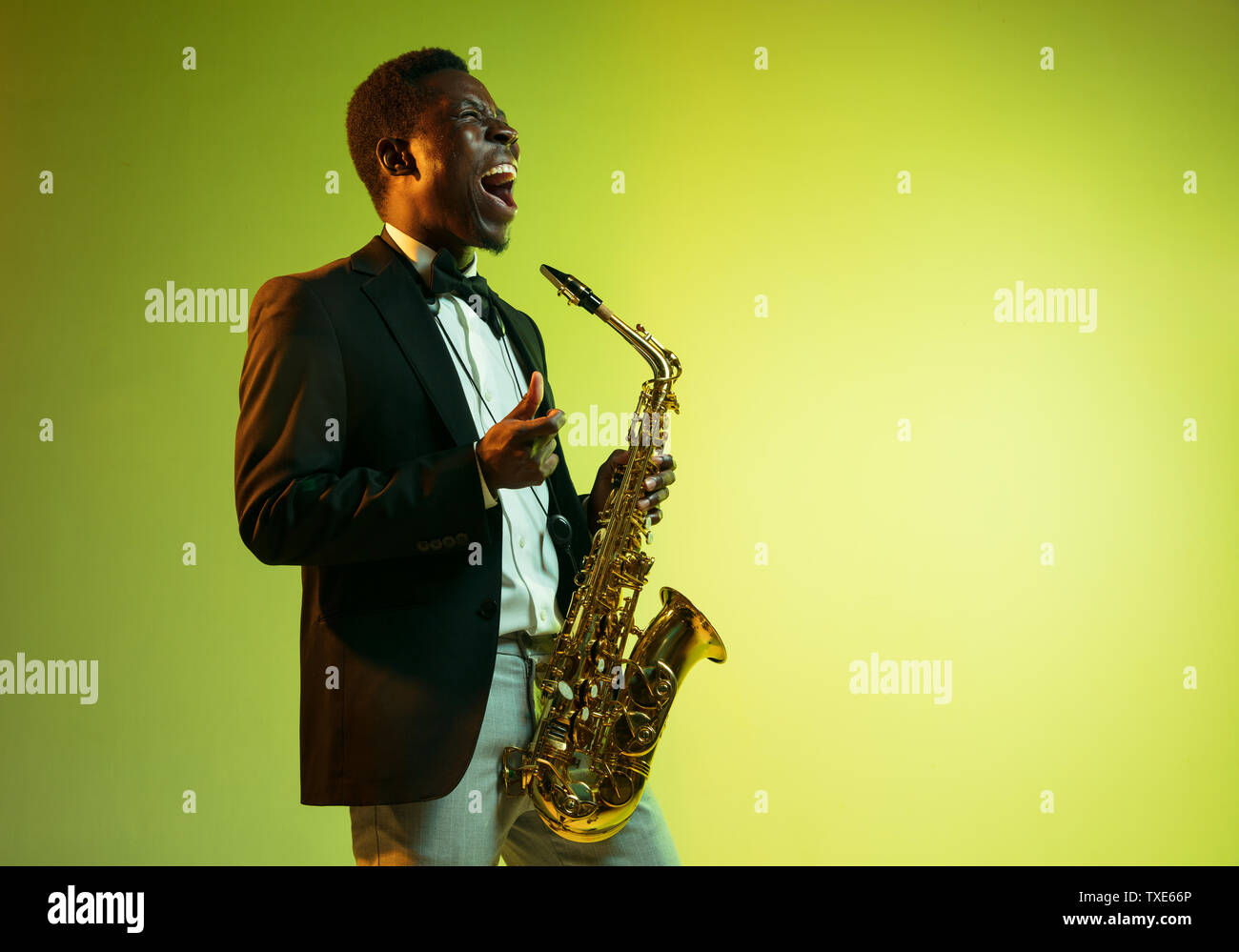 Young african-american jazz musician playing the saxophone on gradient ...