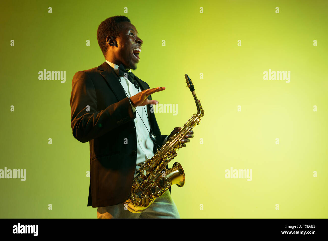Young african-american jazz musician playing the saxophone on gradient ...