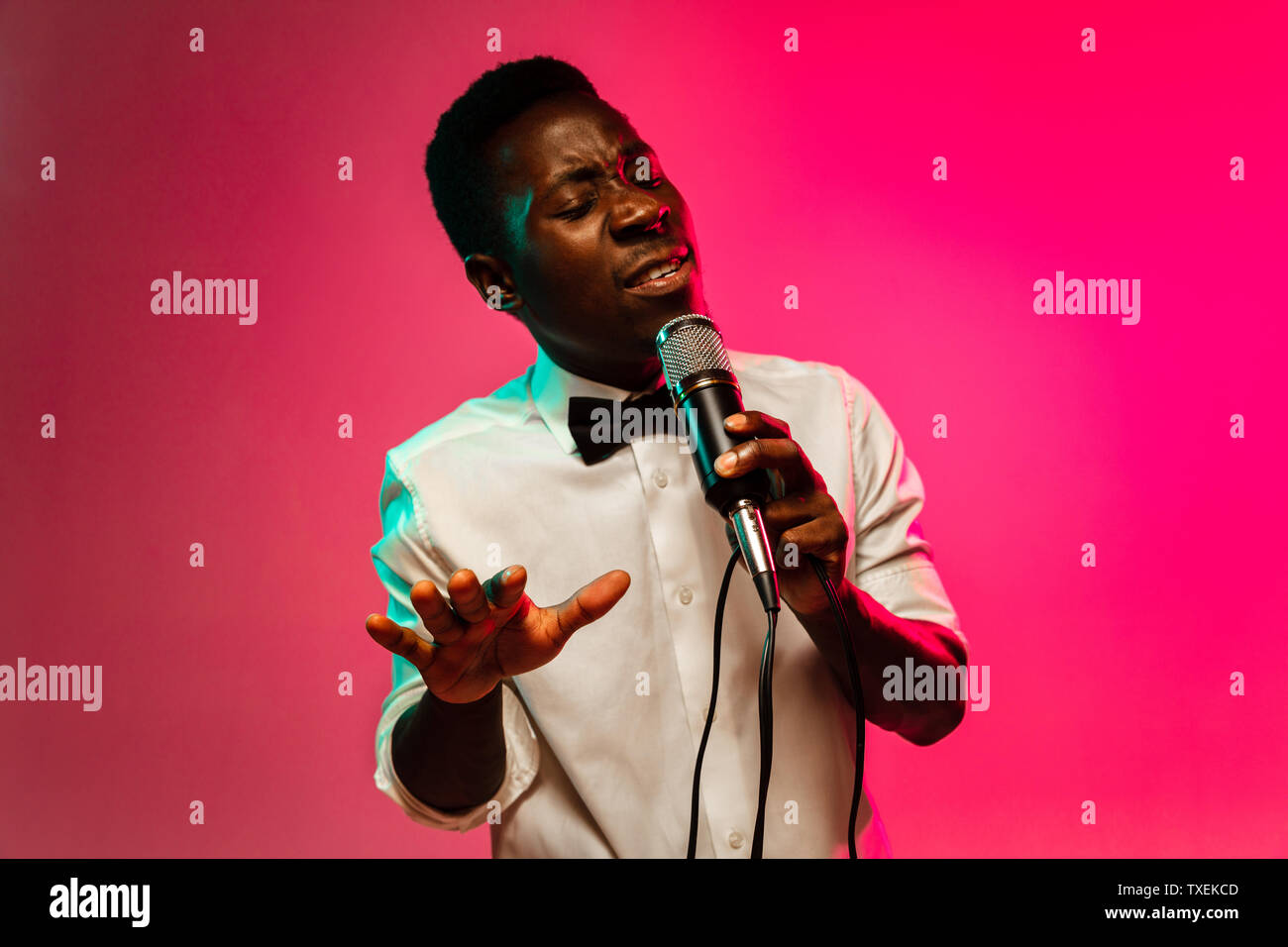 Young african-american jazz musician singing a song on gradient pink ...