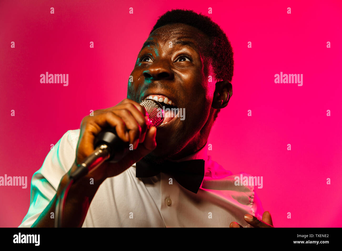 Young african-american jazz musician singing a song on gradient pink ...