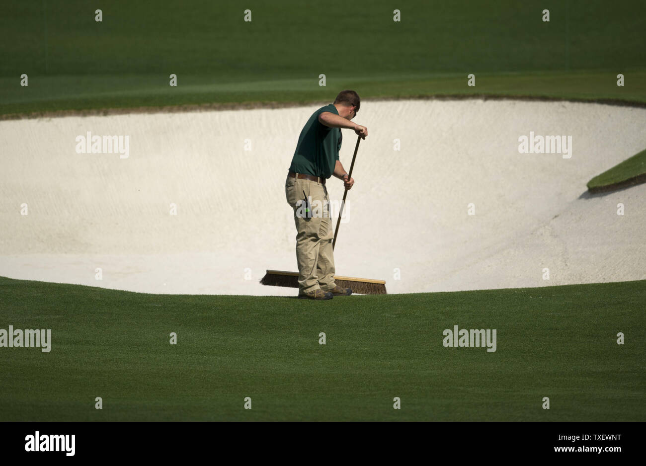 A member of the grounds crew sweeps the sand trap on the 2nd hole ...