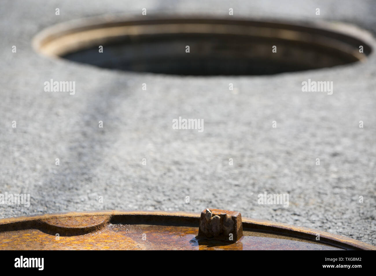 A manhole cover with a cut bolt lays on the ground next to an open ...
