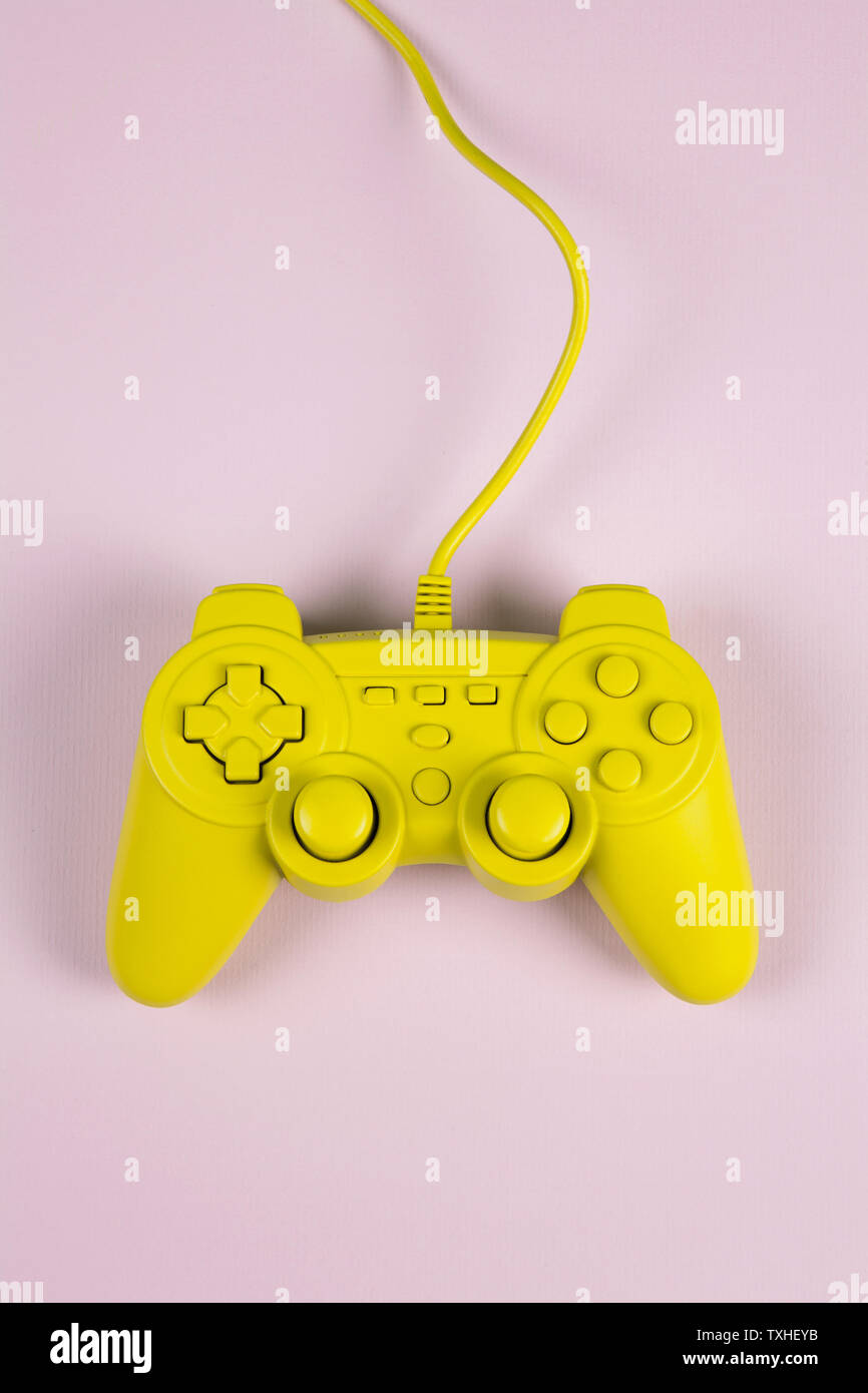 a yellow painted video game controller on a plain pink background ...