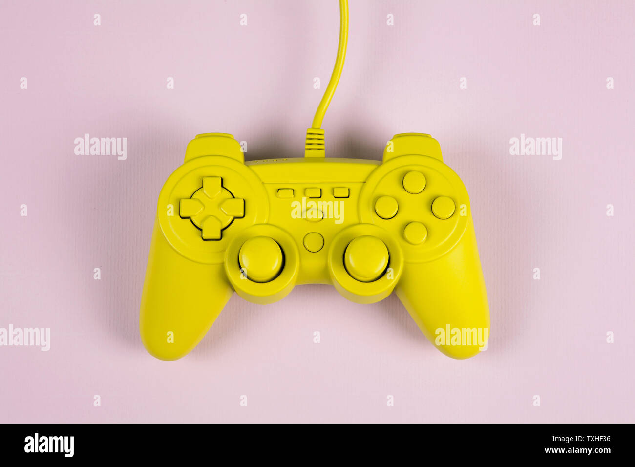 a yellow painted video game controller on a plain pink background ...
