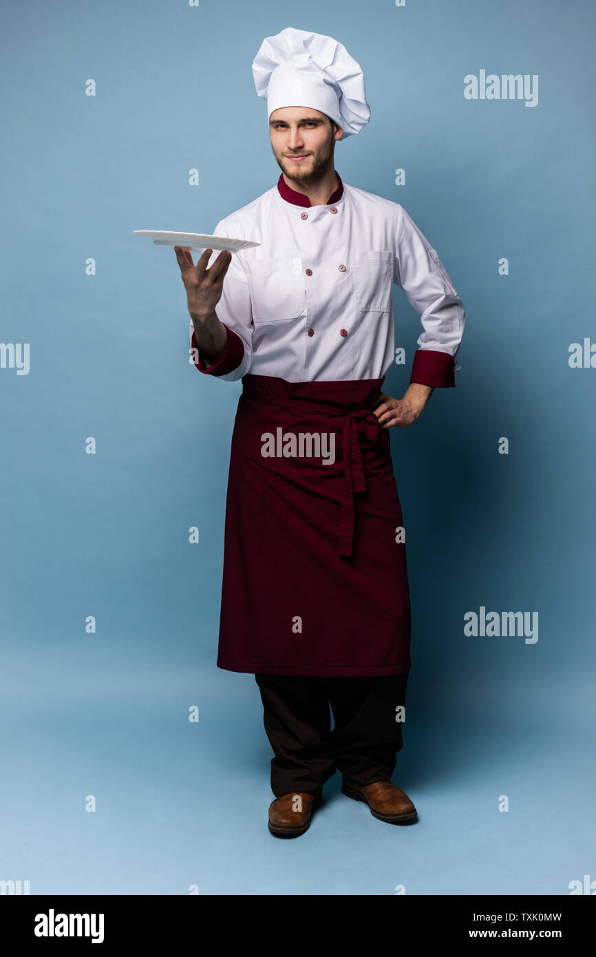 Happy male chef cook standing with plate isolated on light blue ...