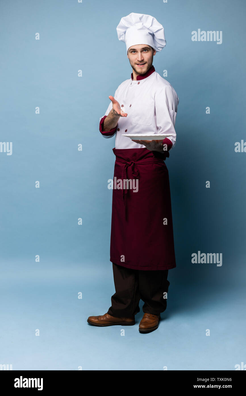 Happy male chef cook standing with plate isolated on light blue ...