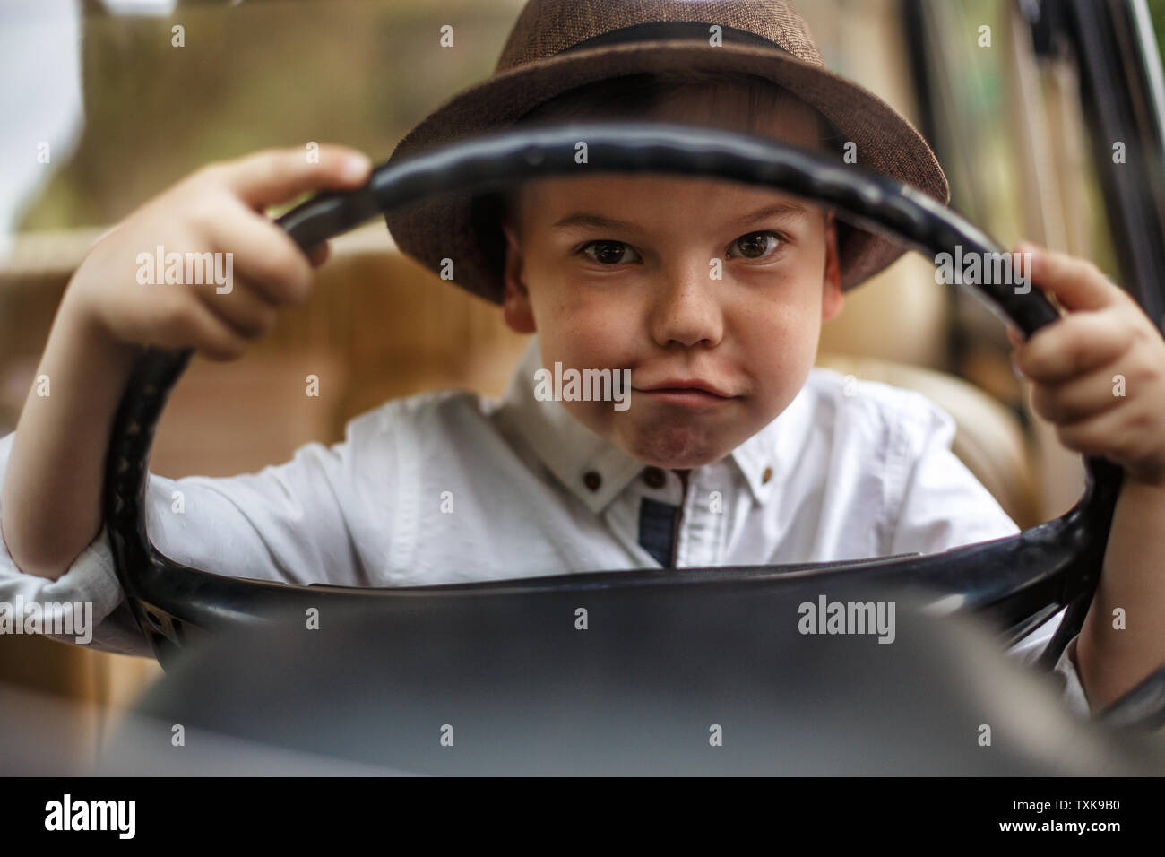 Caucasian little boy in vintage clothes sitting inside a retro car ...
