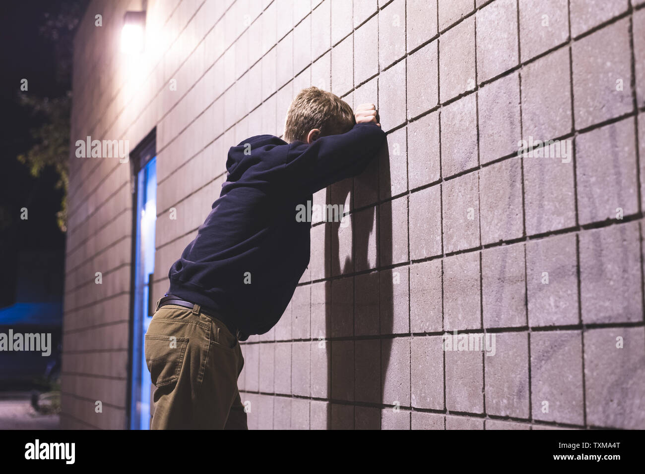 Upset teenager leaning against a brick wall in an alleyway. He is ...