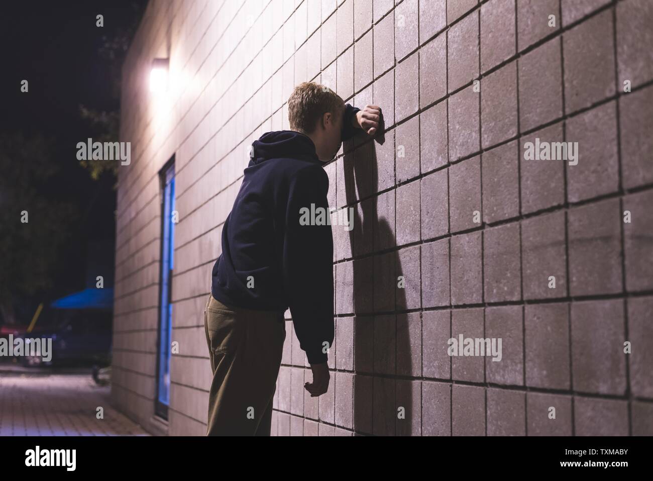 Upset teenager leaning against a brick wall in an alleyway. He is ...