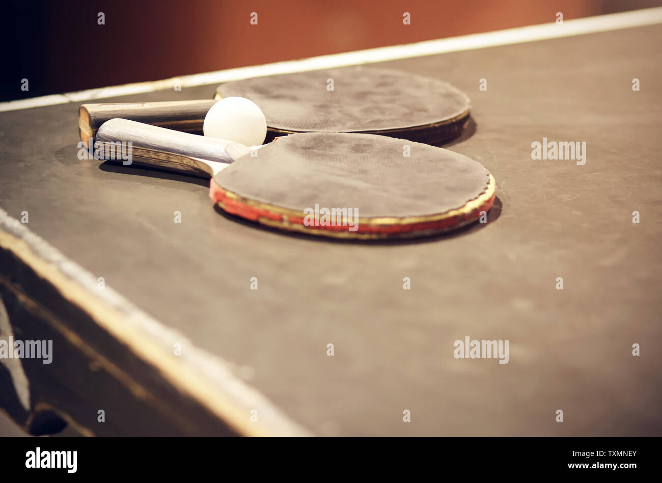 Two worn red and gray ping-pong rackets and a white plastic ball lie on ...