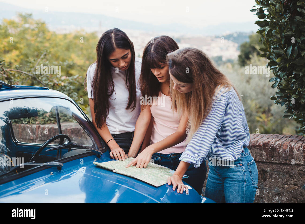 Friends reading route map on car bonnet in countryside Stock Photo - Alamy
