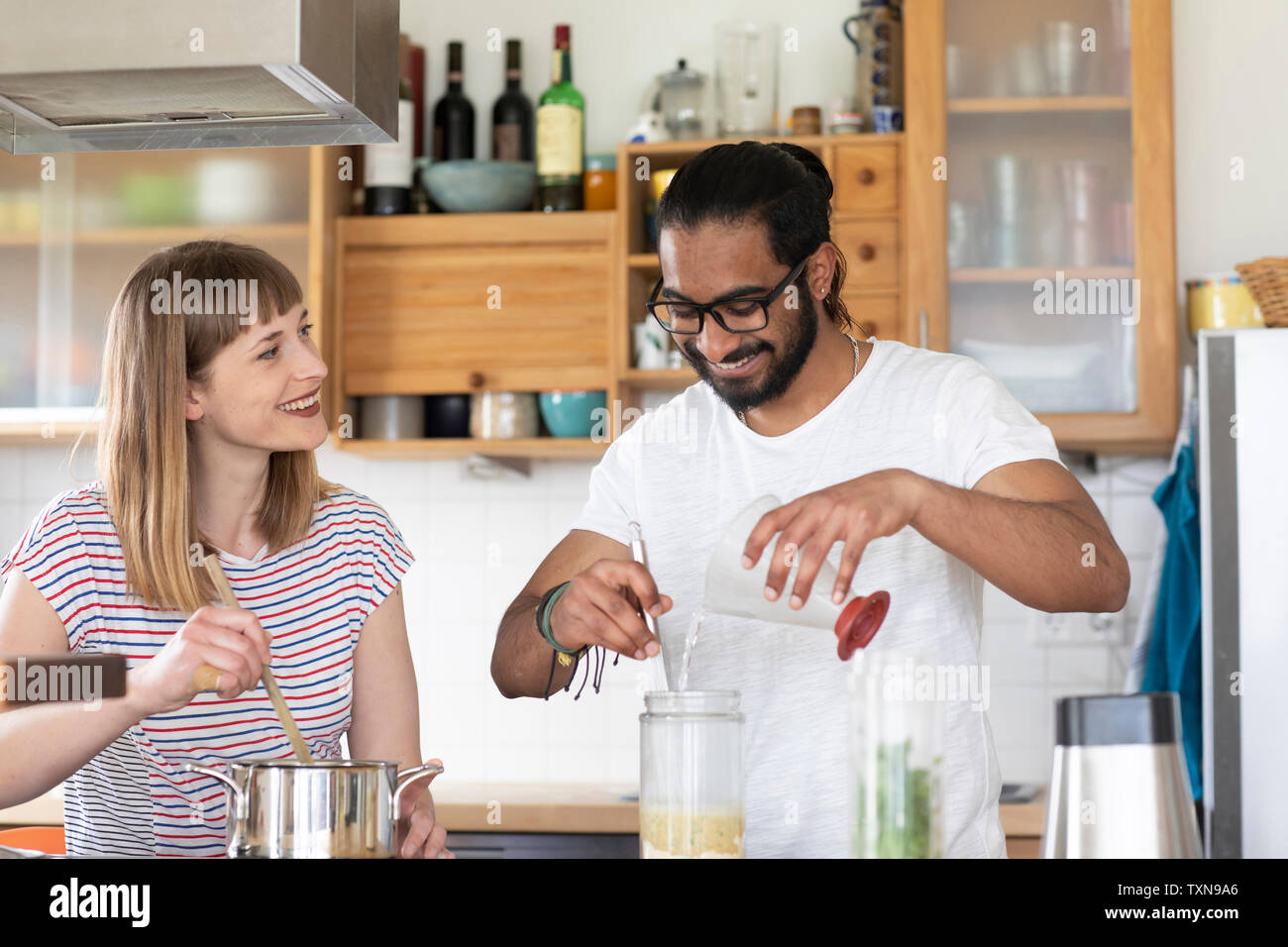 Multi-ethnic couple talking and cooking in kitchen Stock Photo - Alamy