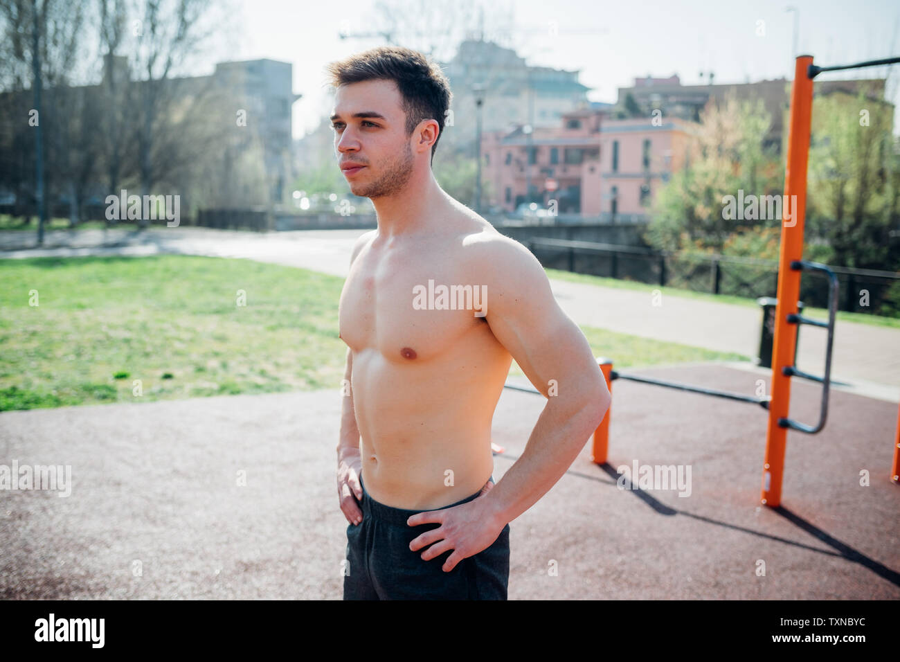 Calisthenics at outdoor gym, bare chested young man taking a break ...