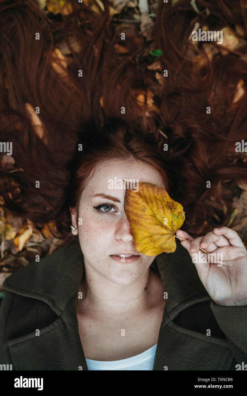 Young Woman With Long Red Hair Lying Amongst Autumn Leaves And Covering