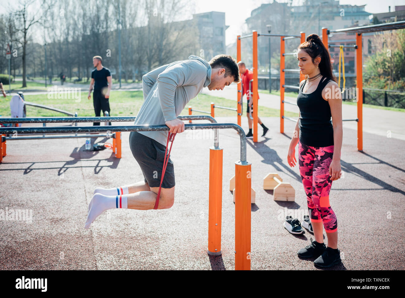 Calisthenics at outdoor gym, trainer watching young man on parallel ...