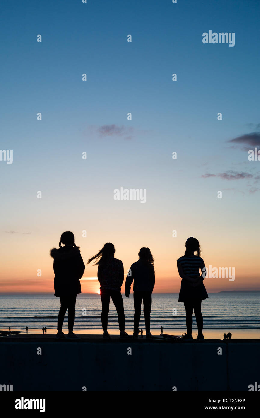 Four children enjoy watching the sunset over the ocean in Devon UK ...