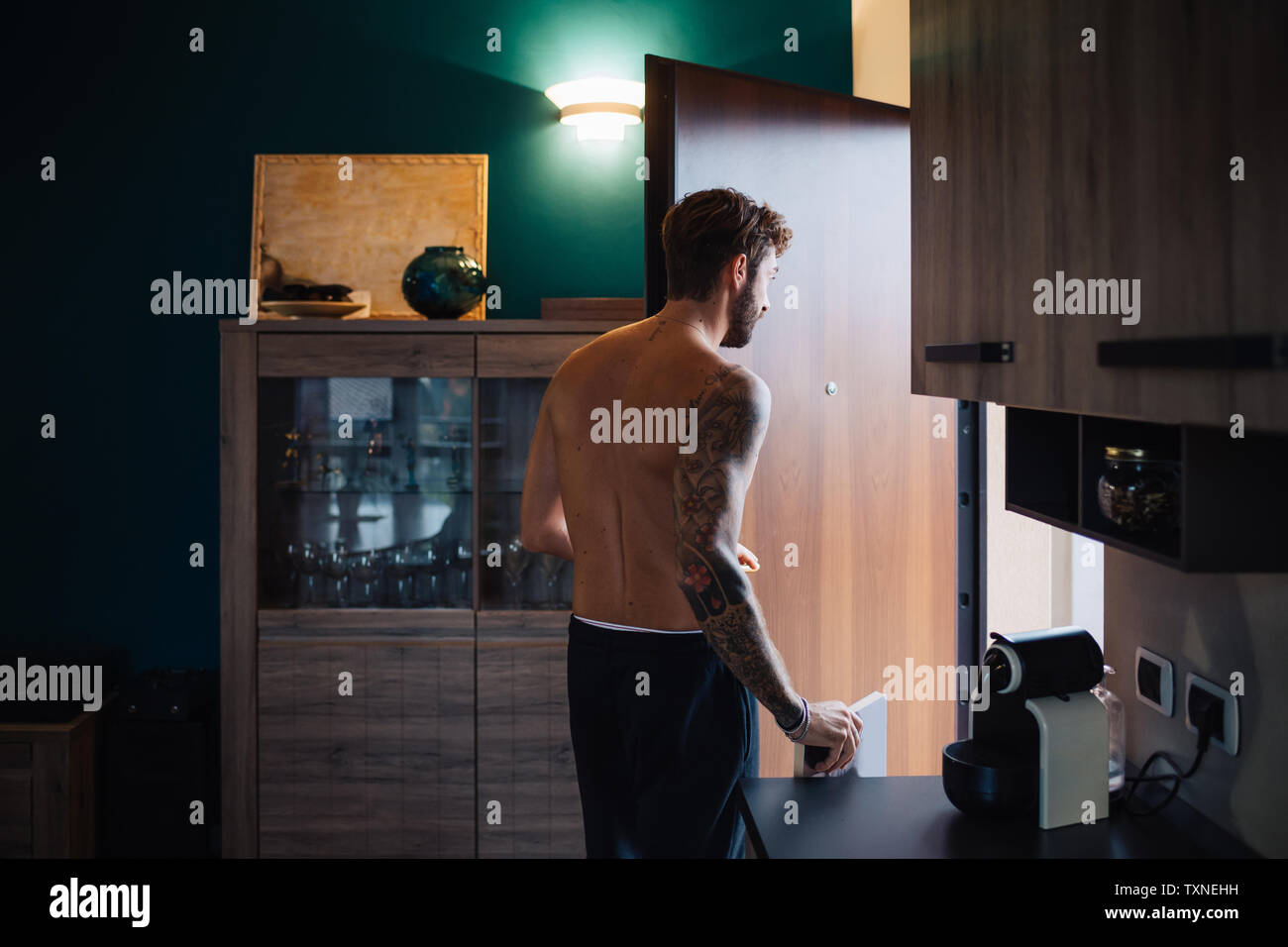 Mid adult man with tattooed arm leaving kitchen, rear view Stock Photo ...