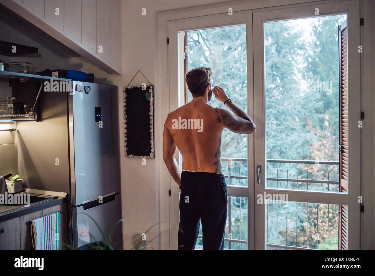 Mid adult man with tattoos drinking coffee and looking out through ...