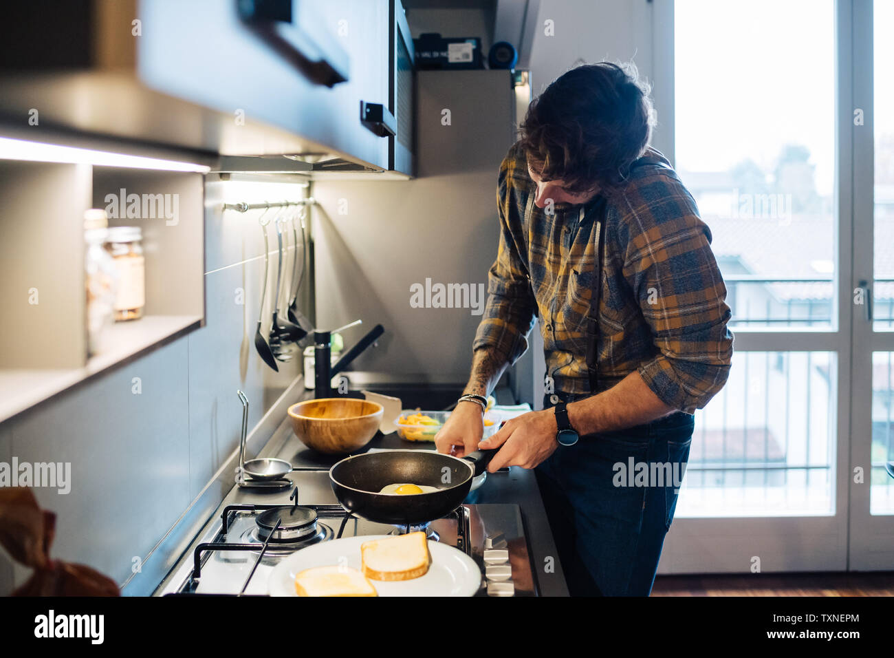 Mid adult man preparing fried eggs at kitchen hob while making ...