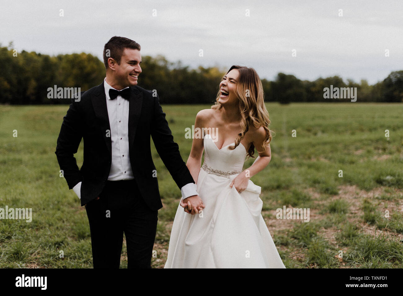 Romantic young bride and groom holding hands and laughing in field ...