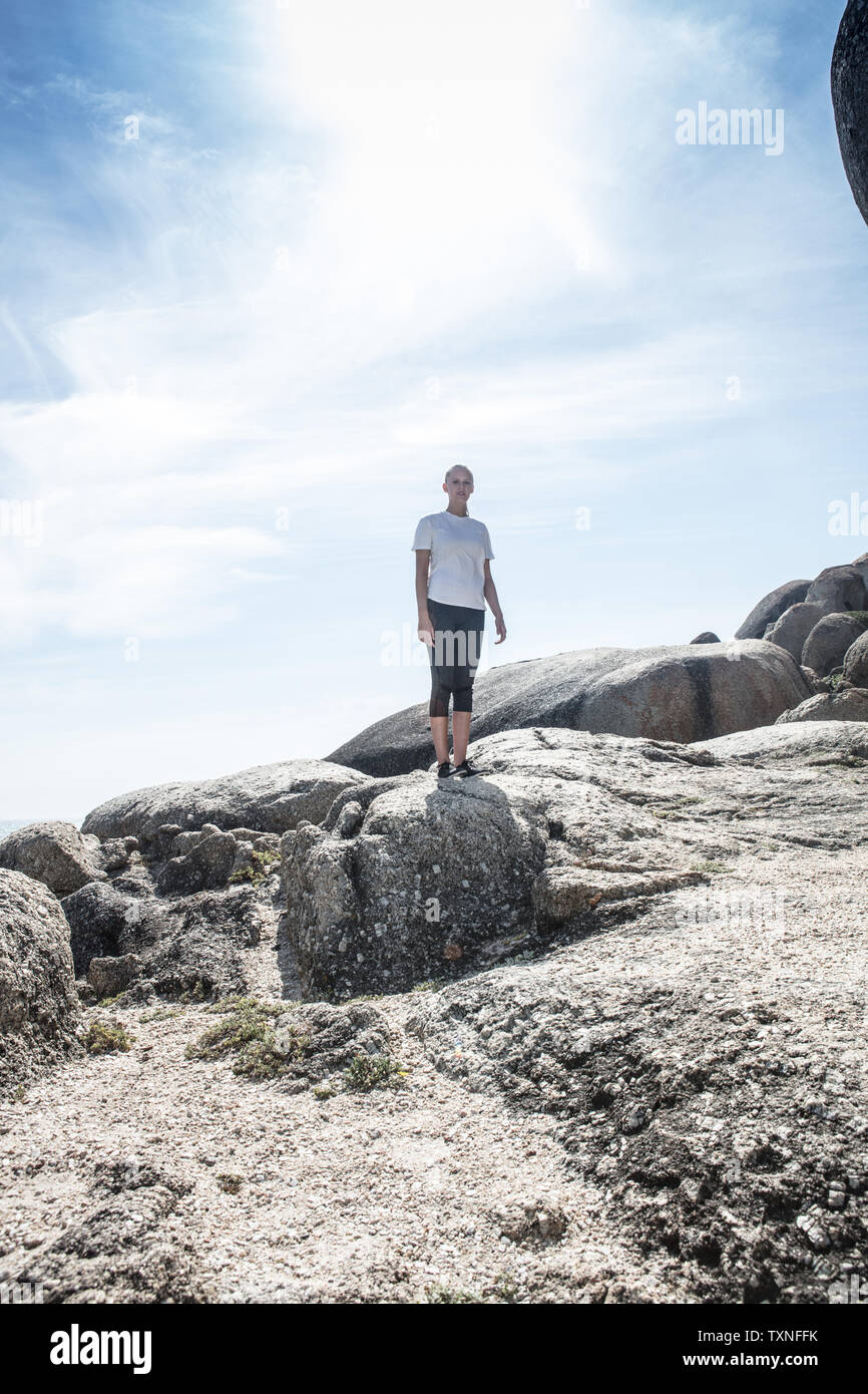Young female runner taking a break on beach rocks, full length, Cape ...