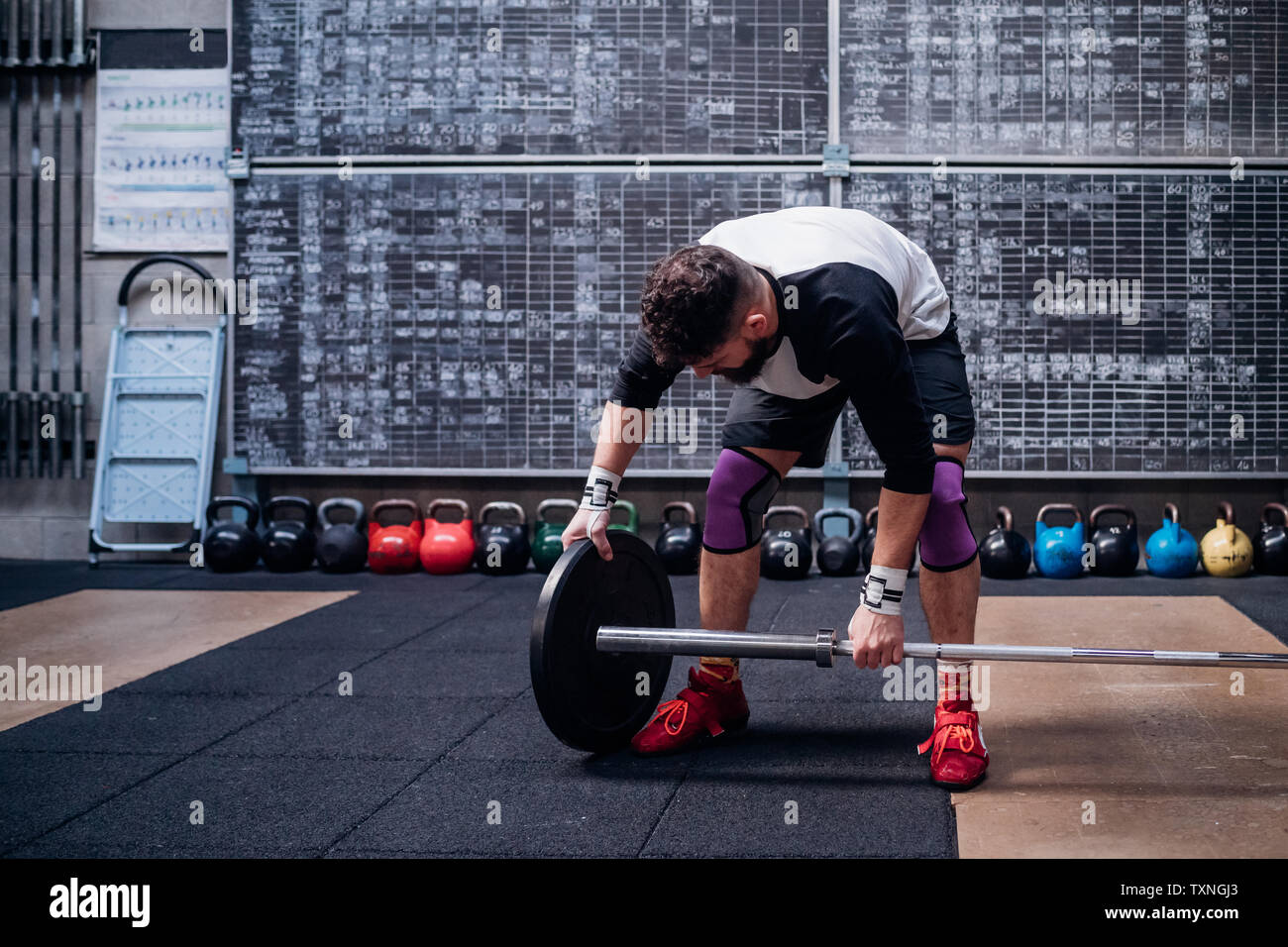 Young man placing weight plate into bar in gym Stock Photo - Alamy