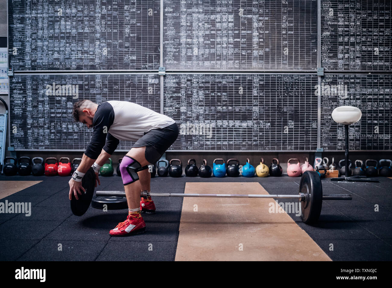 Young man placing weight plate into bar in gym Stock Photo - Alamy